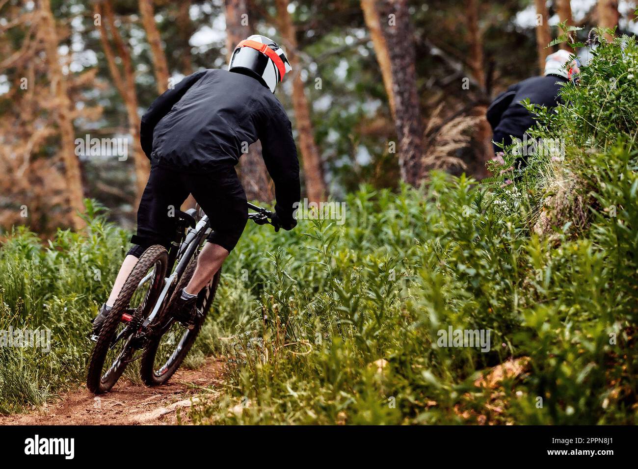rear view male racer riding on forest trail downhill race, black sports ...