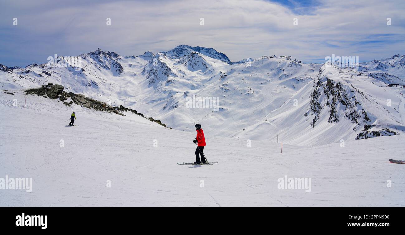 Skier wearing a red jacket and a helmet on a piste passing in front of ...