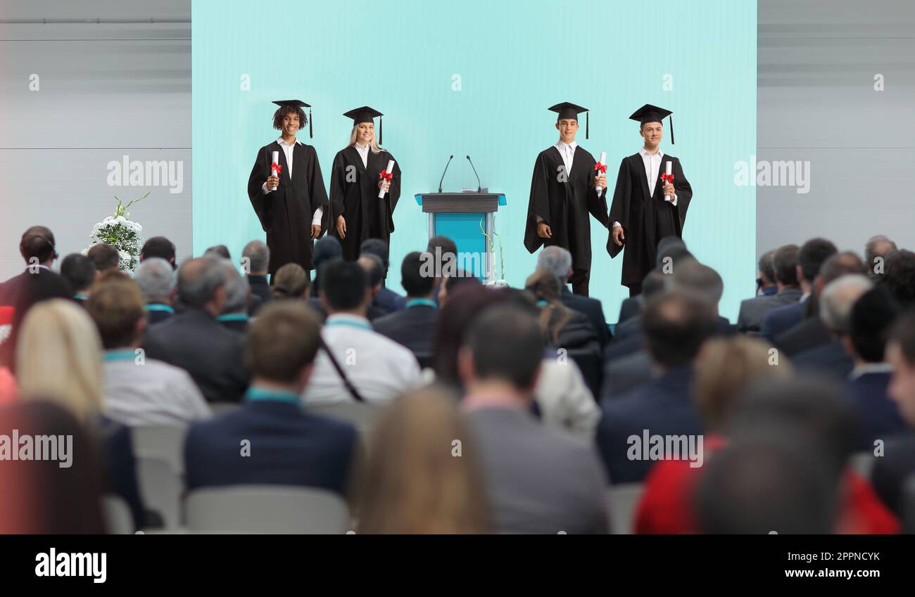 Graduate students holding certificates standing on a podium in front of ...