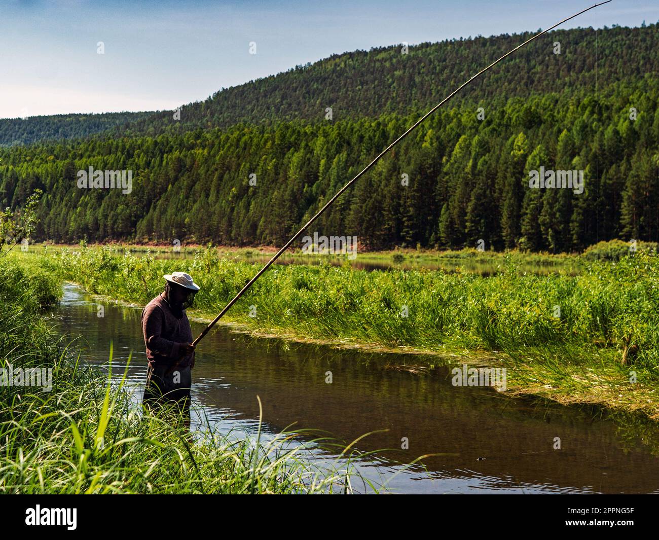 A fisherman stands in the river and catches fish with a wooden fishing ...