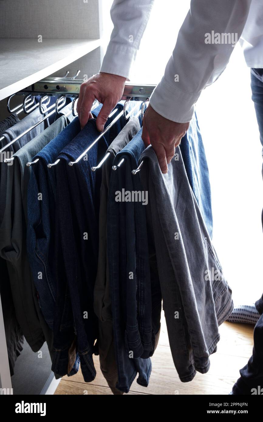 A young adult male standing in an open closet, selecting a pair of ...