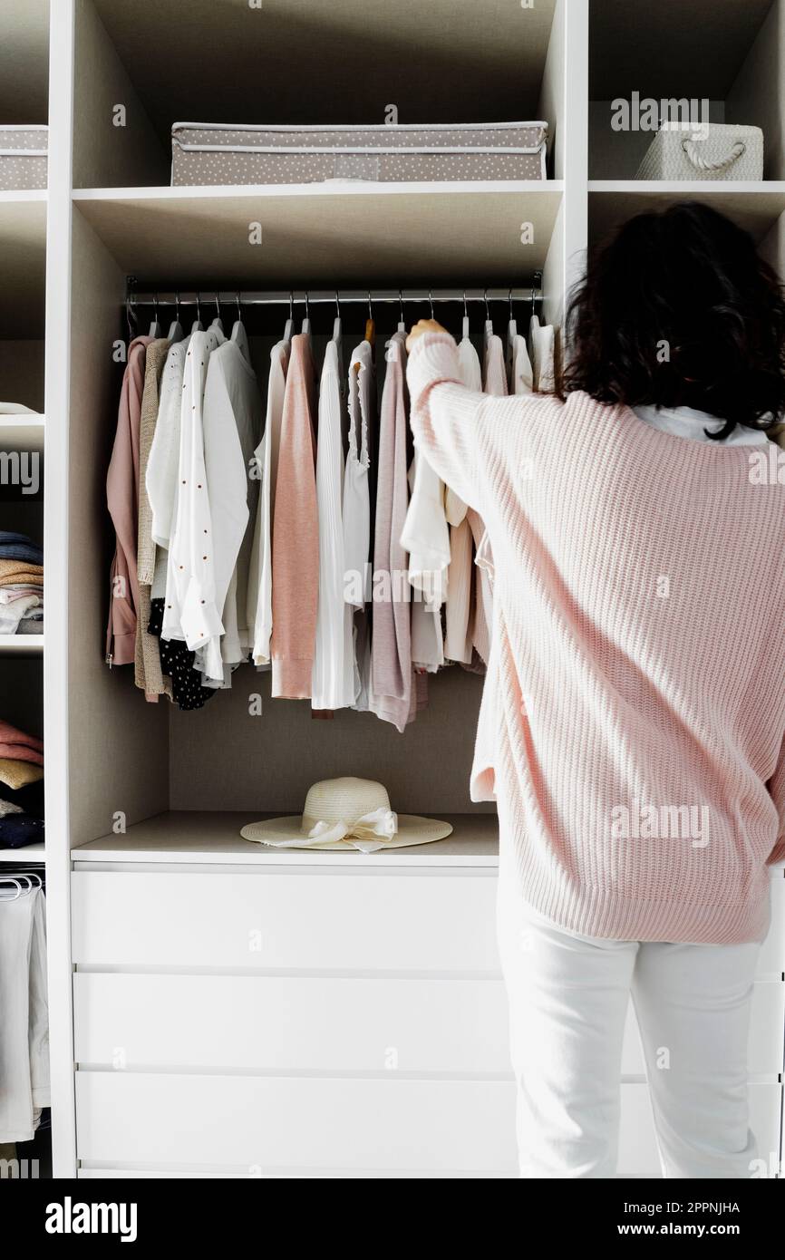 A female is standing in an organized wardrobe with clothes neatly hung ...