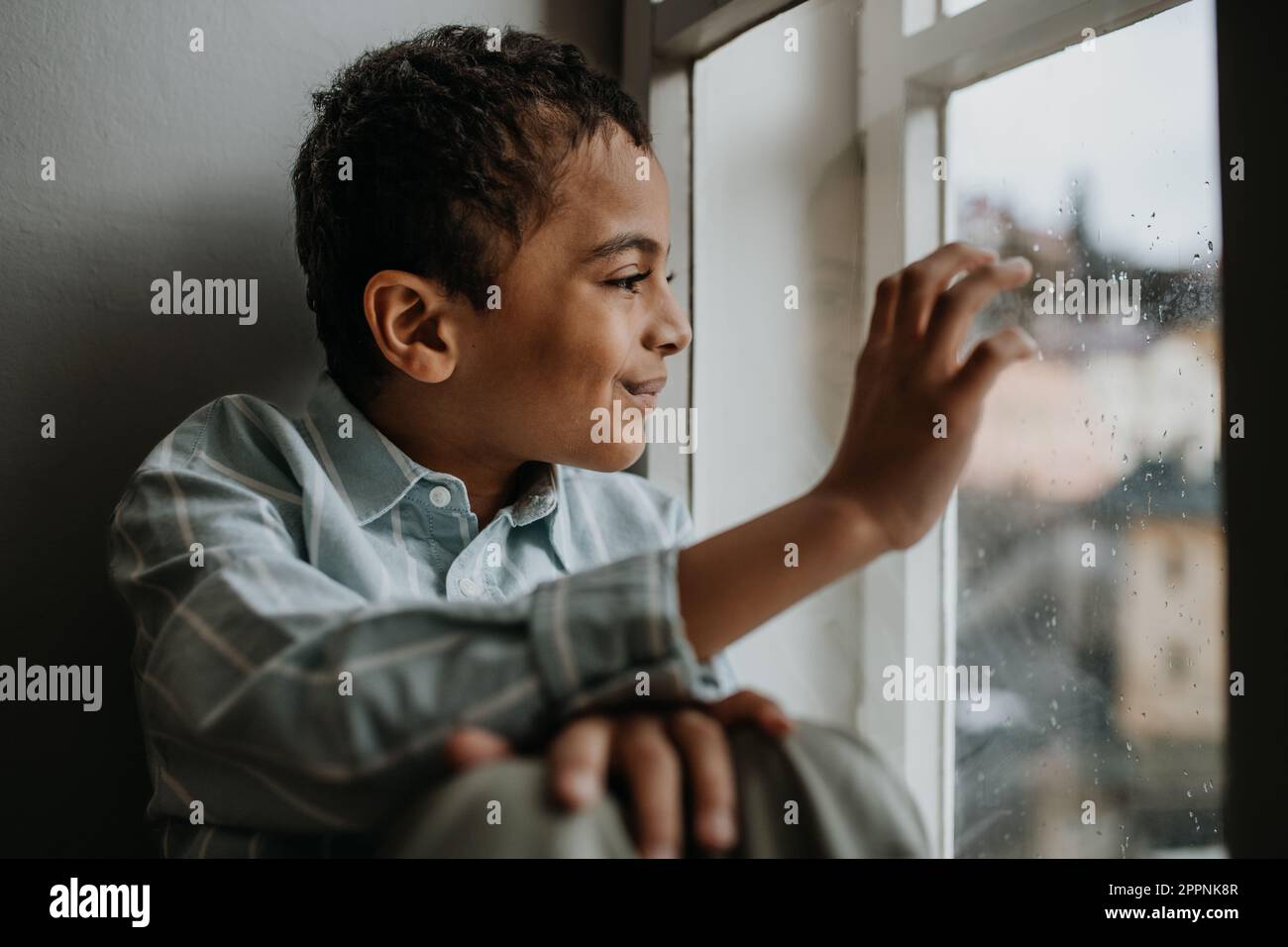 Little multiracial boy looking out of window Stock Photo - Alamy