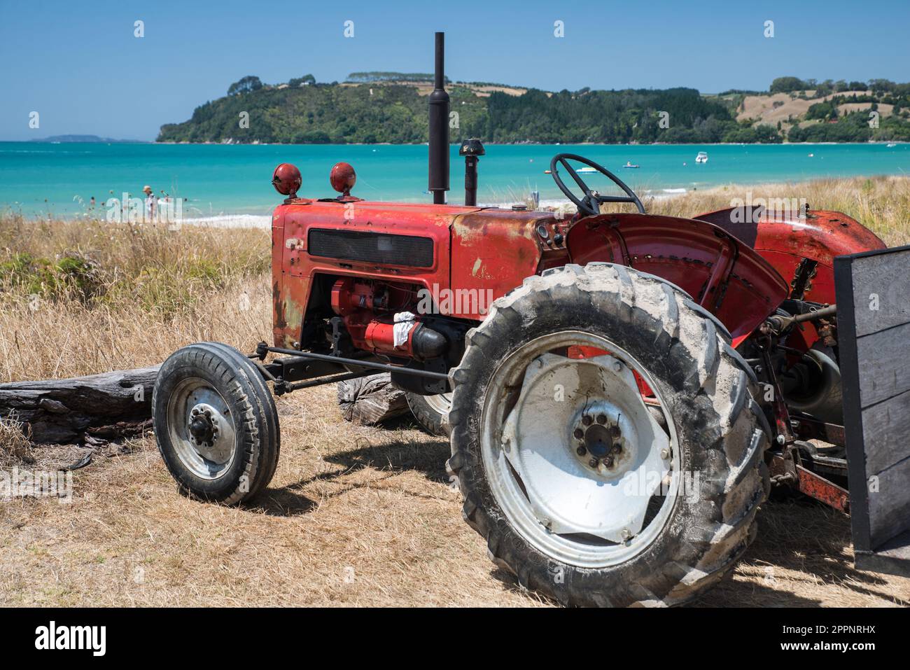 A red 1960s International B-414 tractor parked near a beach on the ...