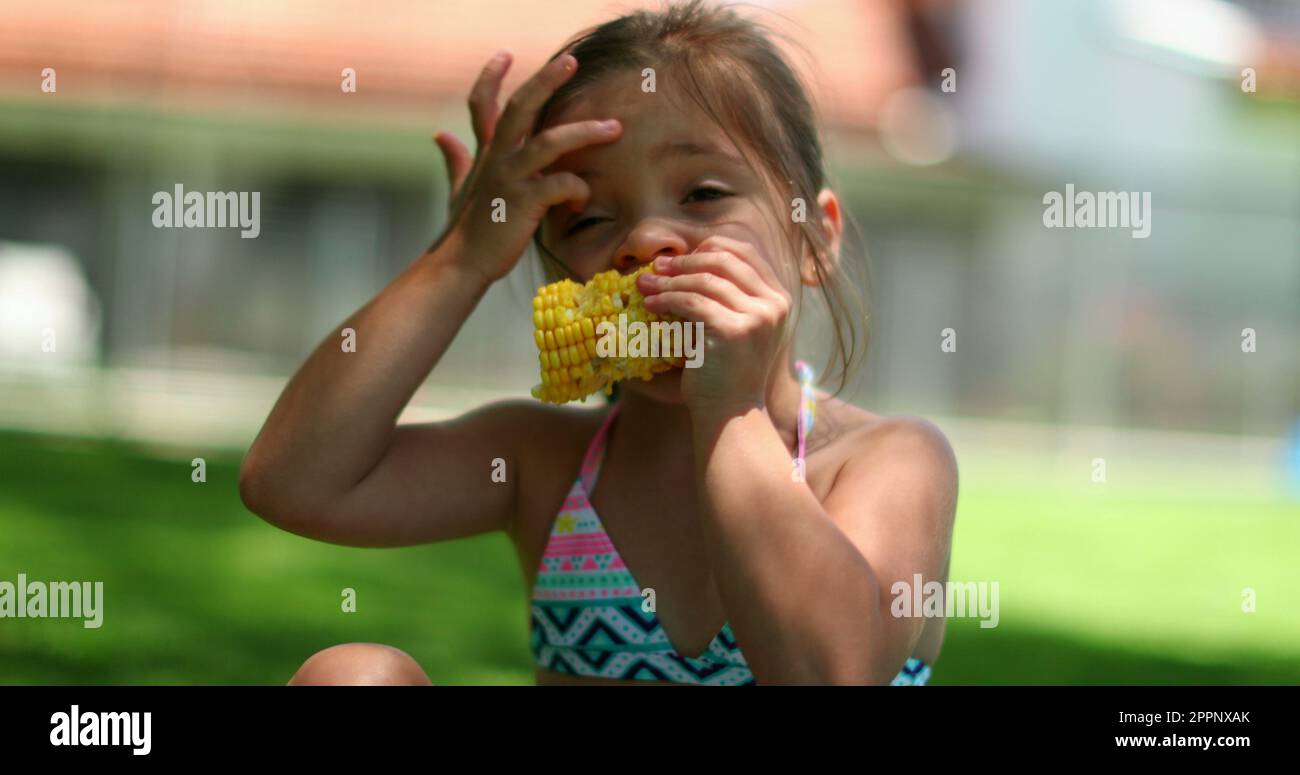 Child eating corn outside in backyard. Little girl kid eats healthy ...