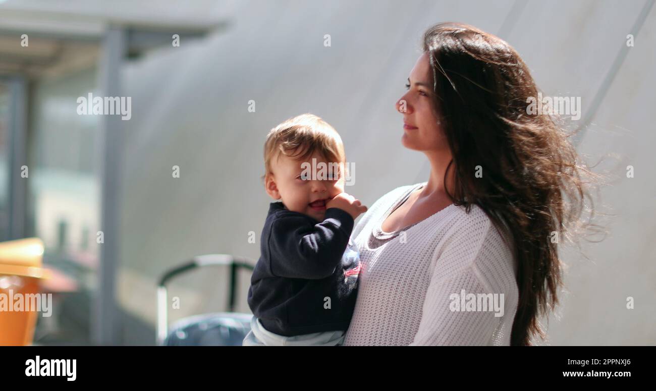 Casual candid mother holding infant baby in arms while waiting for ...