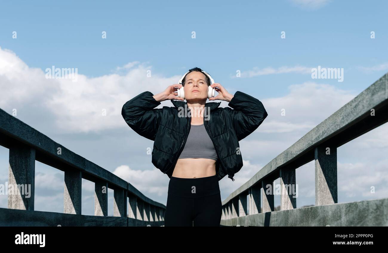 fit, sporty, mid adult woman standing wearing wireless headphones and ...