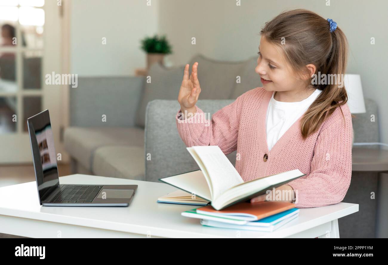 Smiling european teenager girl doing homework and reading book, waving ...