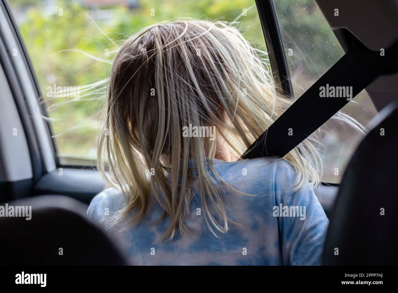 Rear view of teenage sitting in car looking throw open window on ...