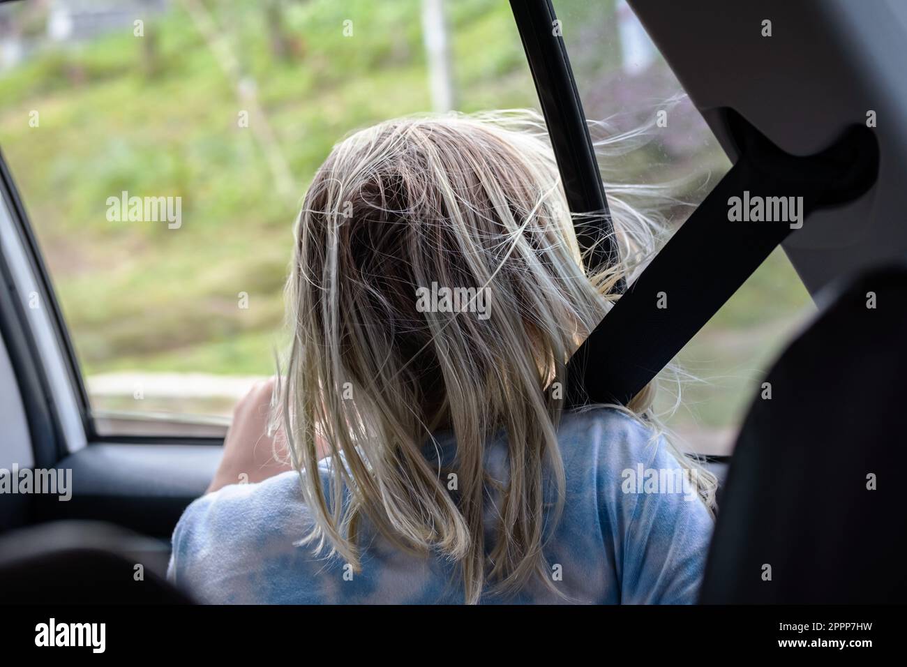 Rear view of teenage sitting in car looking throw open window on ...