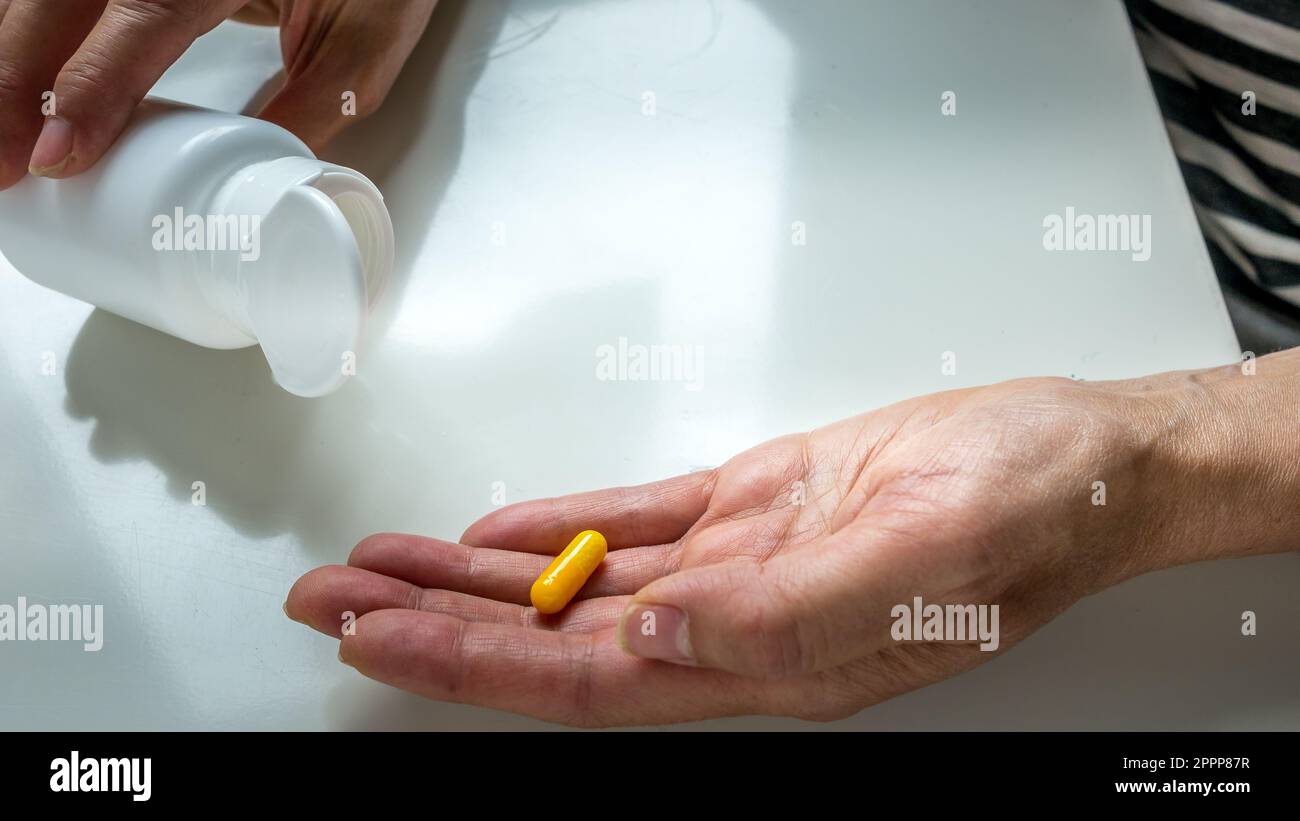 Hand with a yellow pill, coated capsule, dosing a medication from a ...