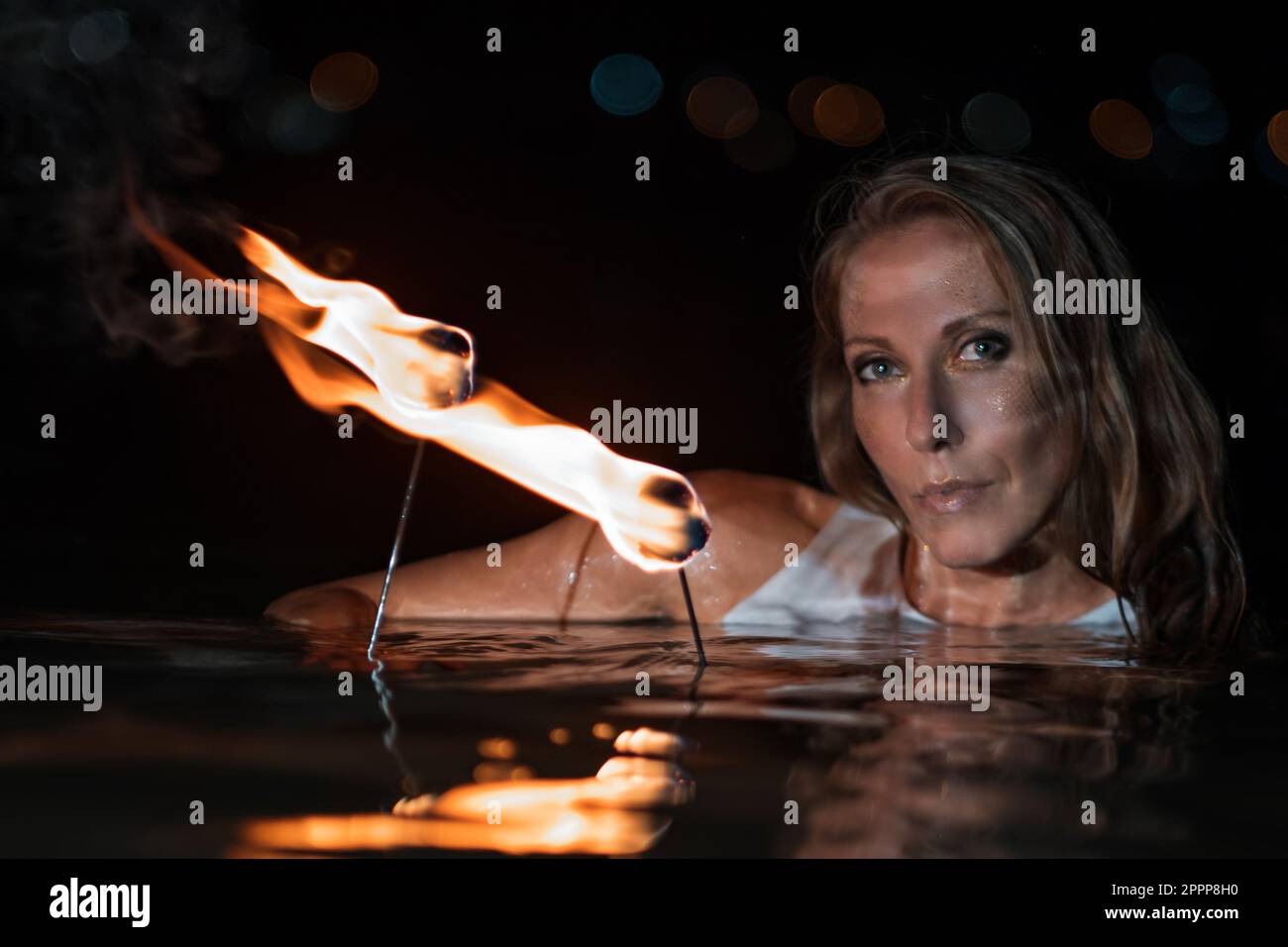 Caucasian woman dancing with fire in the water. Fire show at sea ...