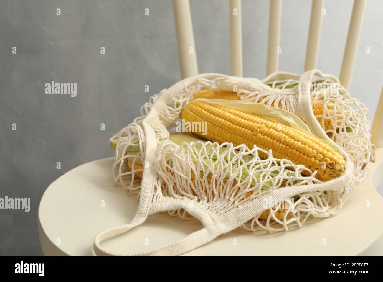 Bag of corn cobs on chair against grey background Stock Photo - Alamy