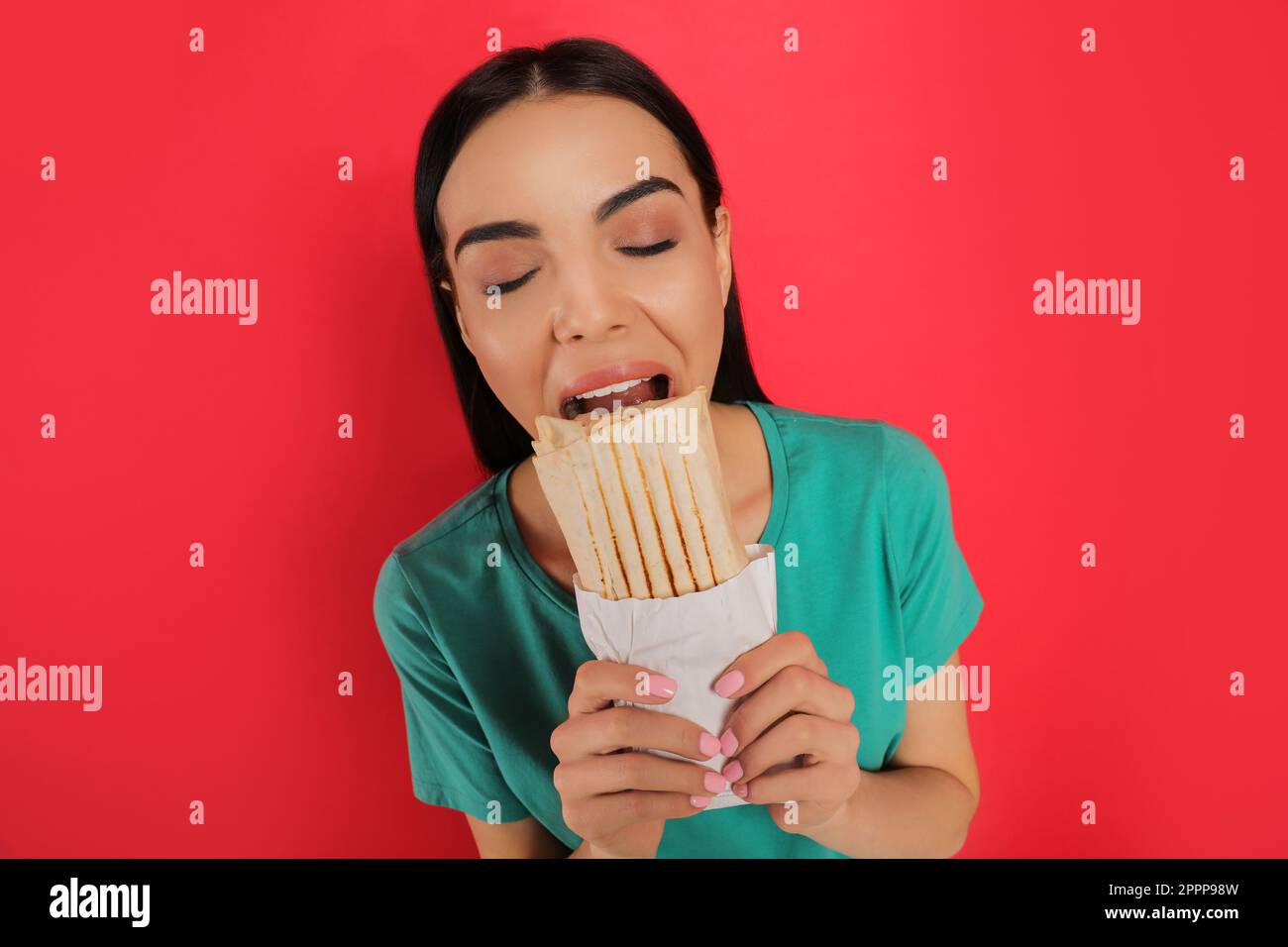 Young woman eating delicious shawarma on red background Stock Photo - Alamy