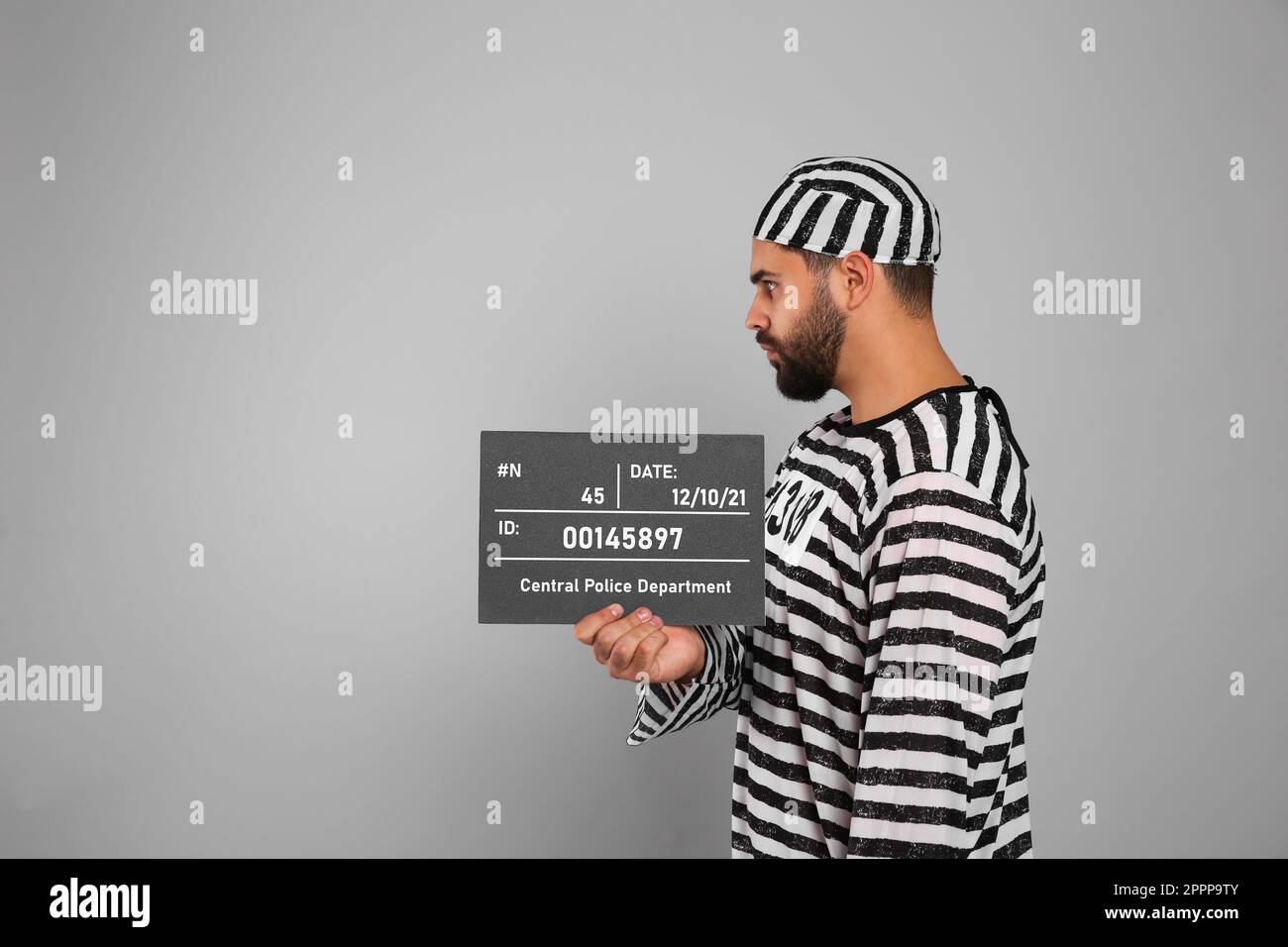 Prisoner in special uniform with mugshot letter board on grey ...