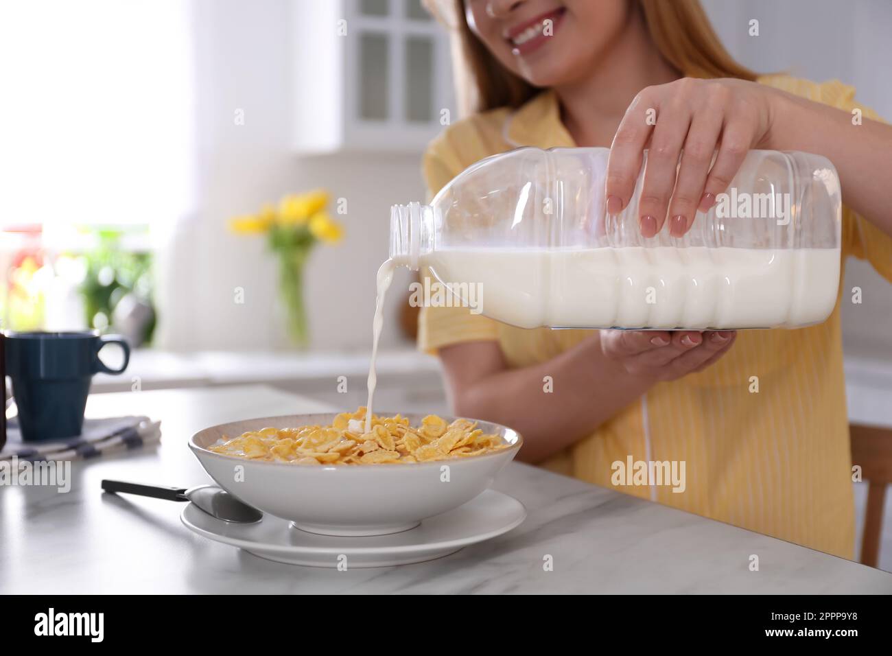 Young woman pouring milk from gallon bottle into plate with breakfast ...