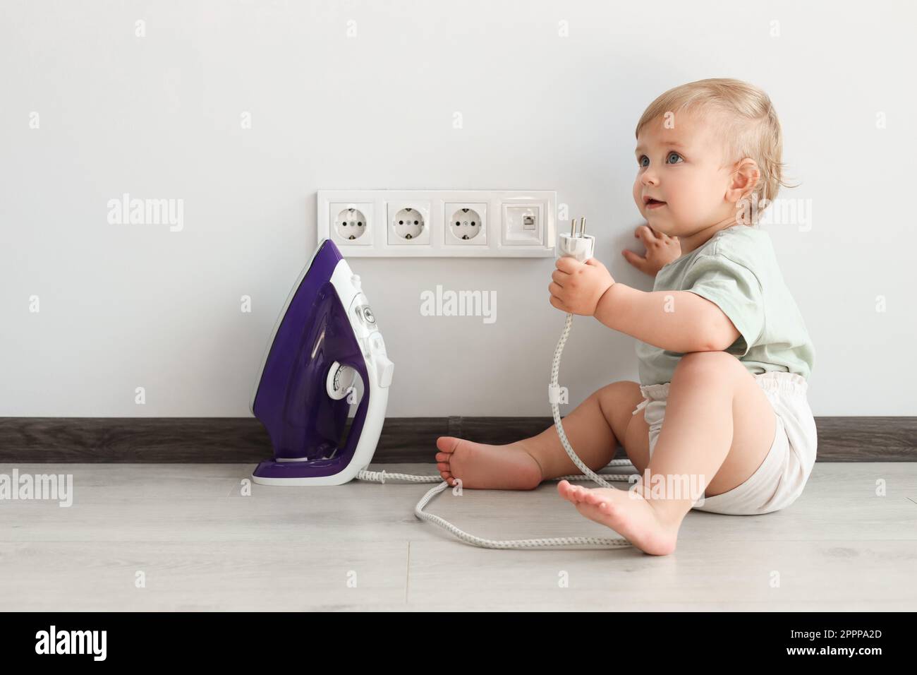 Cute baby playing with electrical socket and iron plug at home ...