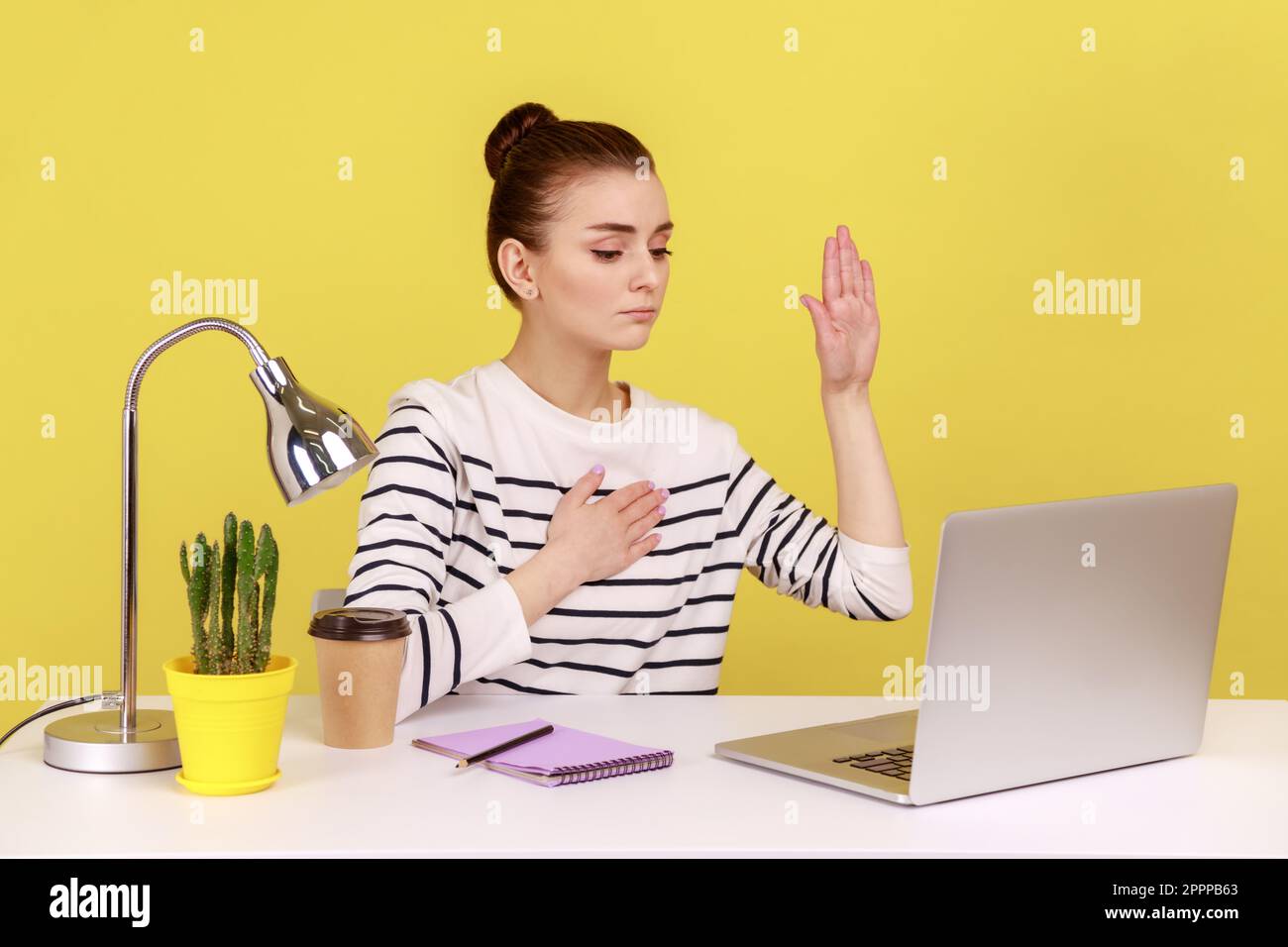 Honest woman sitting at workplace and raising hand to give promise ...