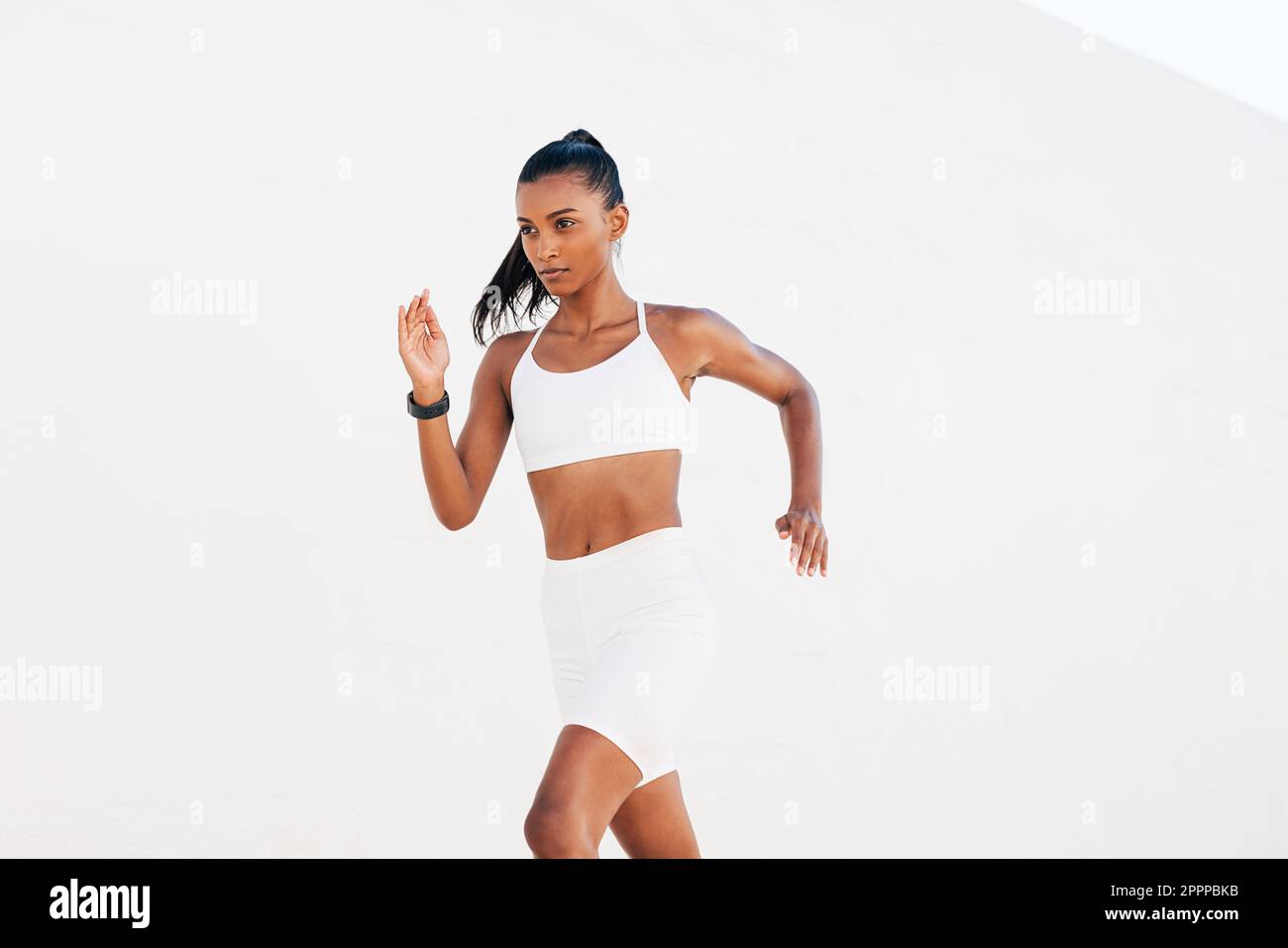 Slim female sprinter exercising outdoors at white wall. Young slim ...