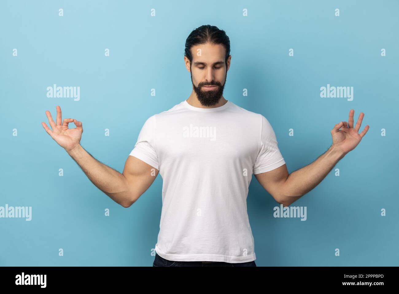 Portrait of calm relaxed man with beard wearing white T-shirt doing ...