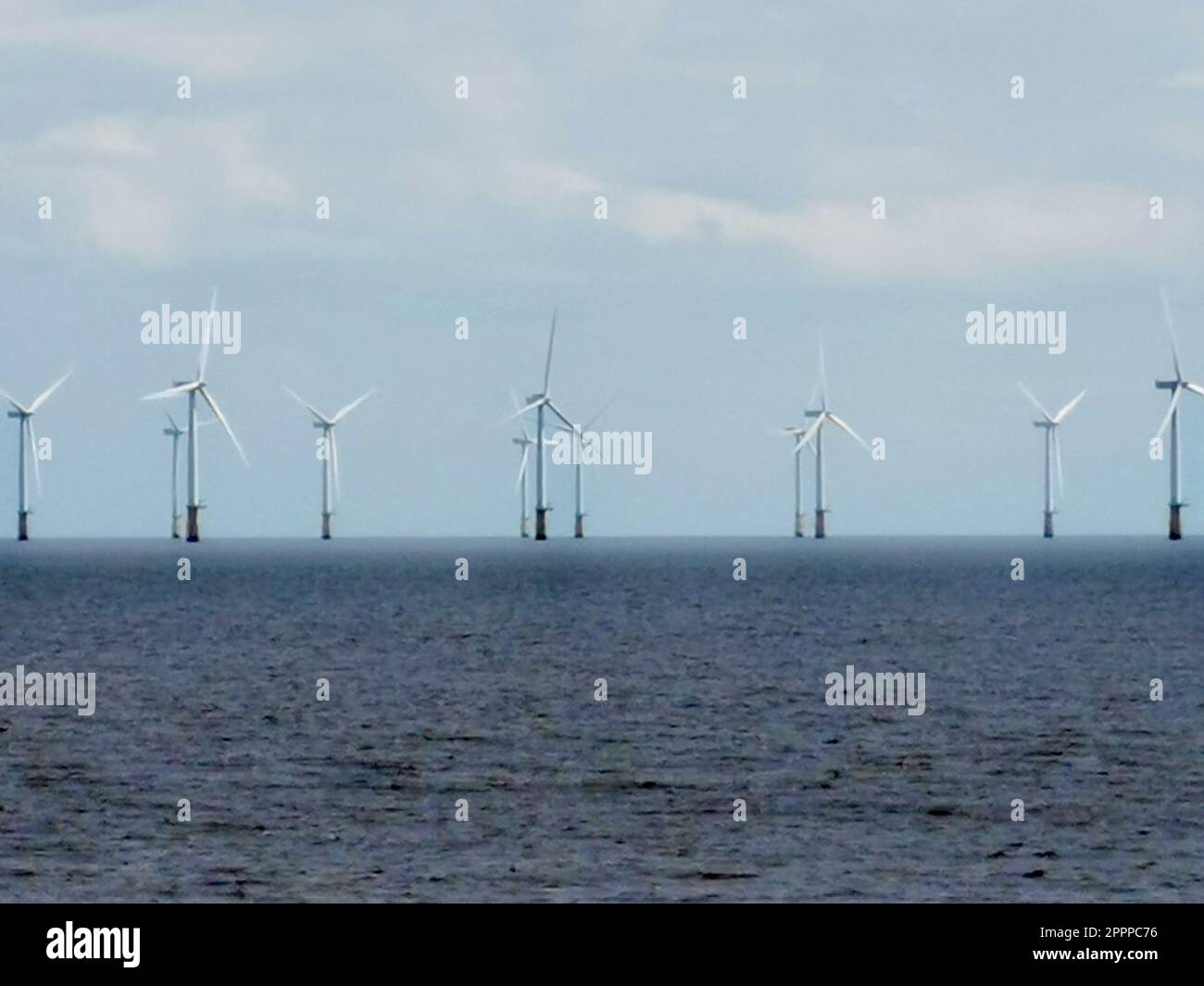 Wind farm on horizon at sea with dark blue sea below and pale blue sky ...
