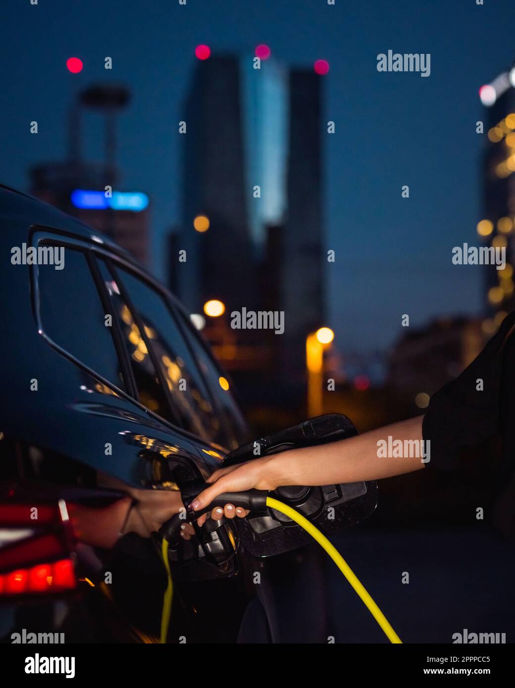 Female hands opening an electric car charging socket cap and plugging ...