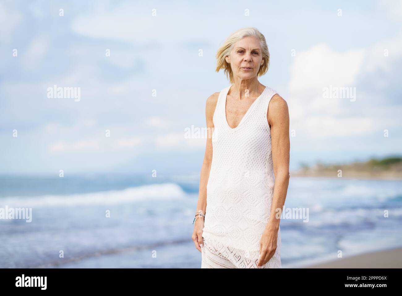 Smiling mature woman walking on the beach. Elderly female standing at a ...