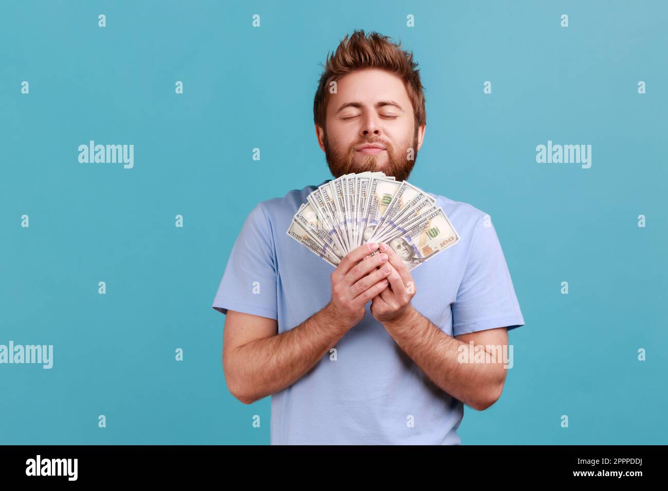 Portrait of satisfied bearded man smelling earned dollar banknotes ...