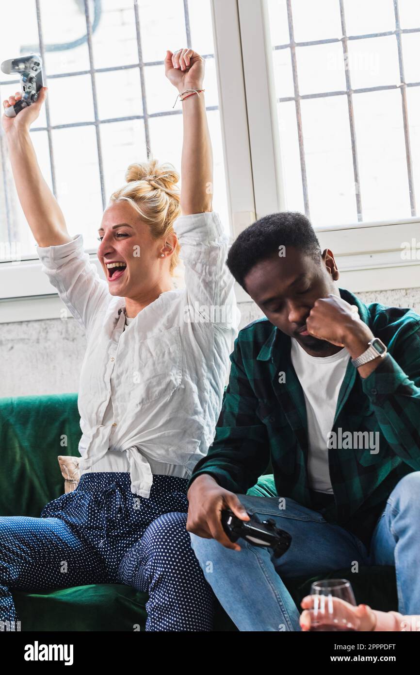 Caucasian girl cheering for winning a game of video games and African ...