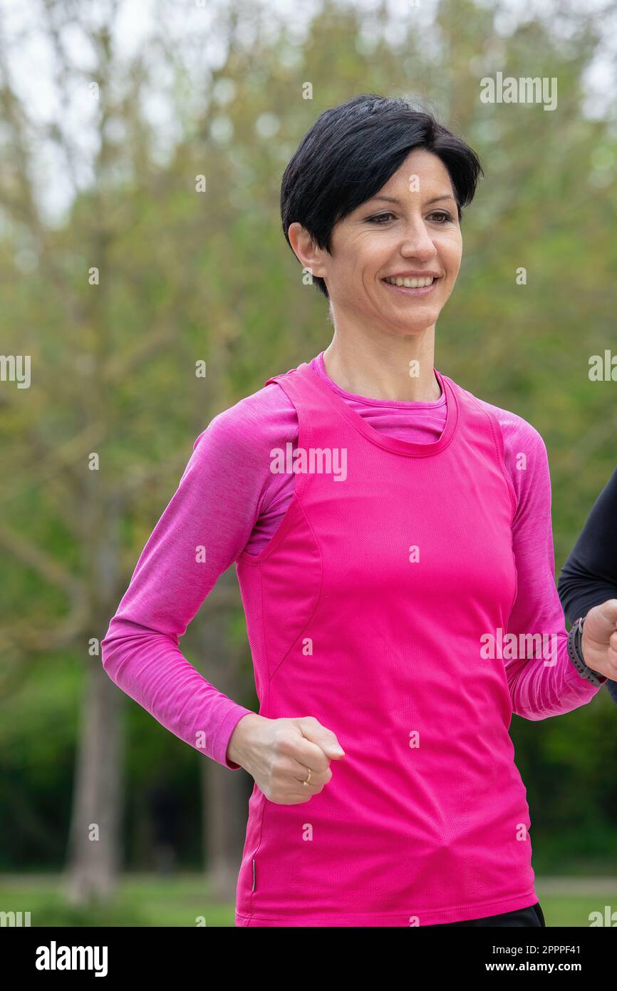 Smiling mature woman with youthful spirit running happy at the park ...