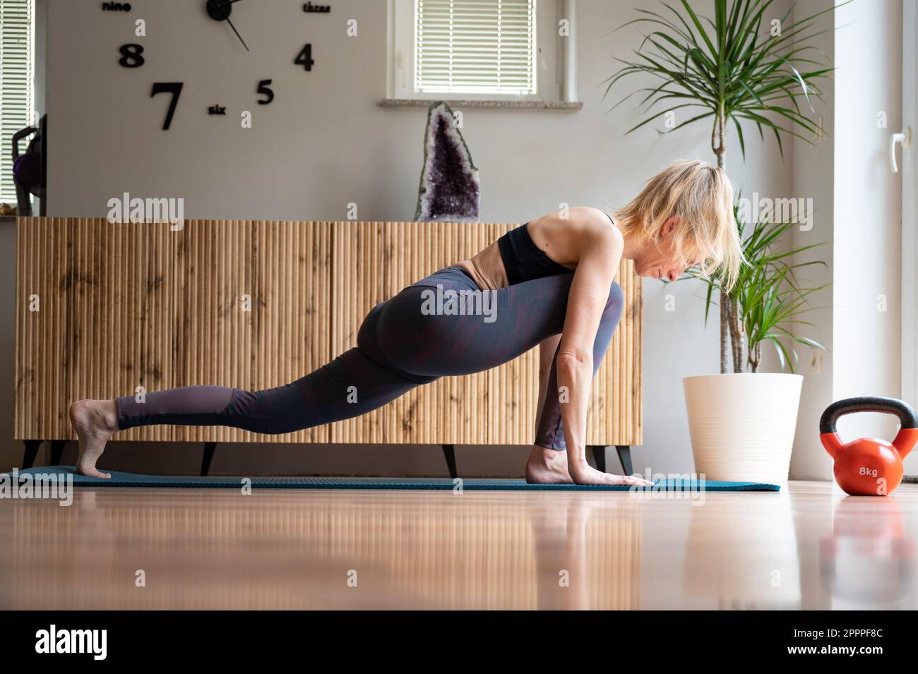 Young woman practicing yoga sun salutation in her living room on an ...