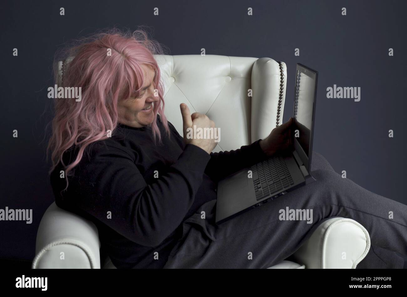 A man in a pink wig sits in a white chair and communicates via video ...