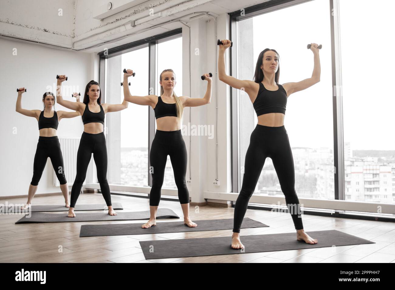 Group of young women in activewear taking up standing pose on mats ...