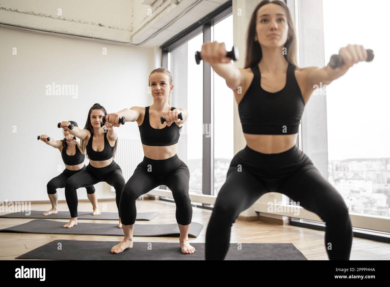 Young female athletes in yoga outfit holding dumbbells while doing ...