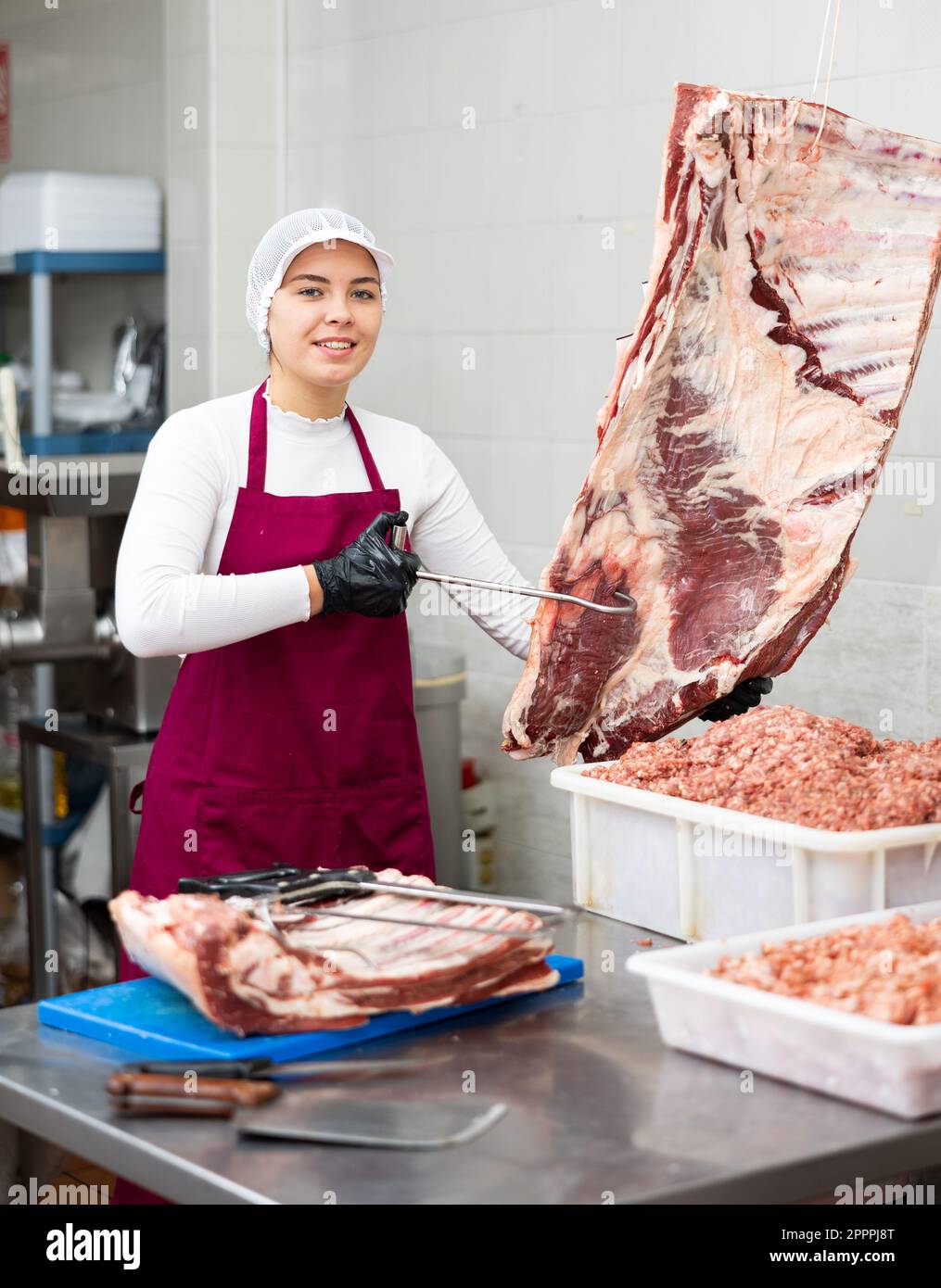 Happy female butcher showing big piece of beef ribs in meat section of ...