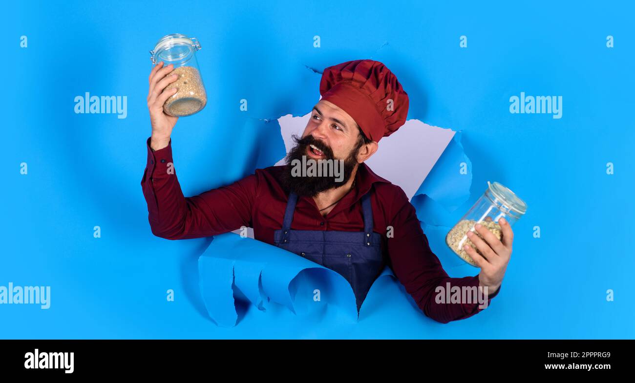Male chef in hat and apron holds jars with cereals looking through ...