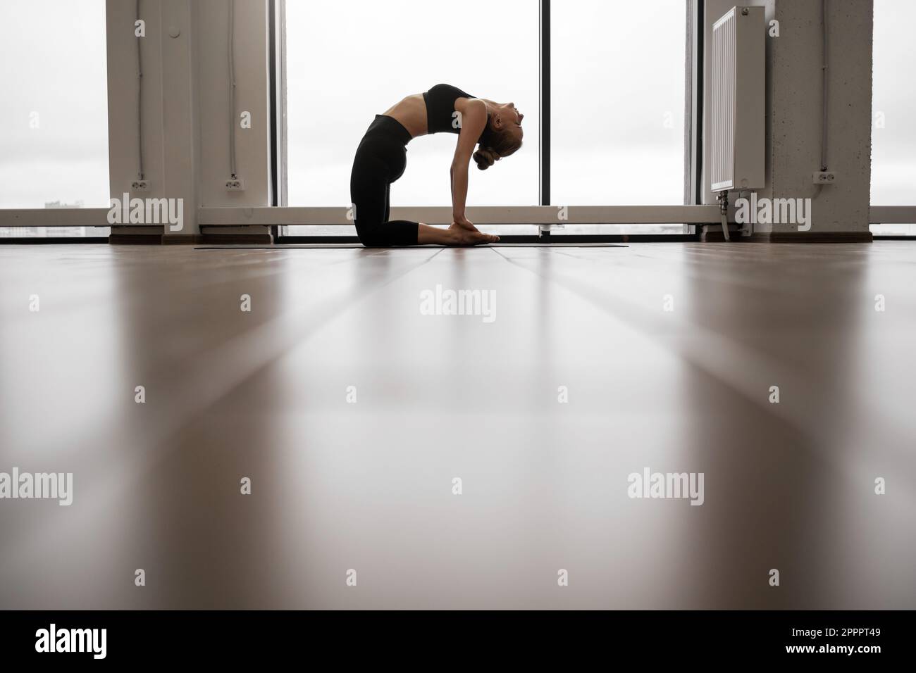 Sporty fit female yogi wearing black crop top and leggings bending back ...