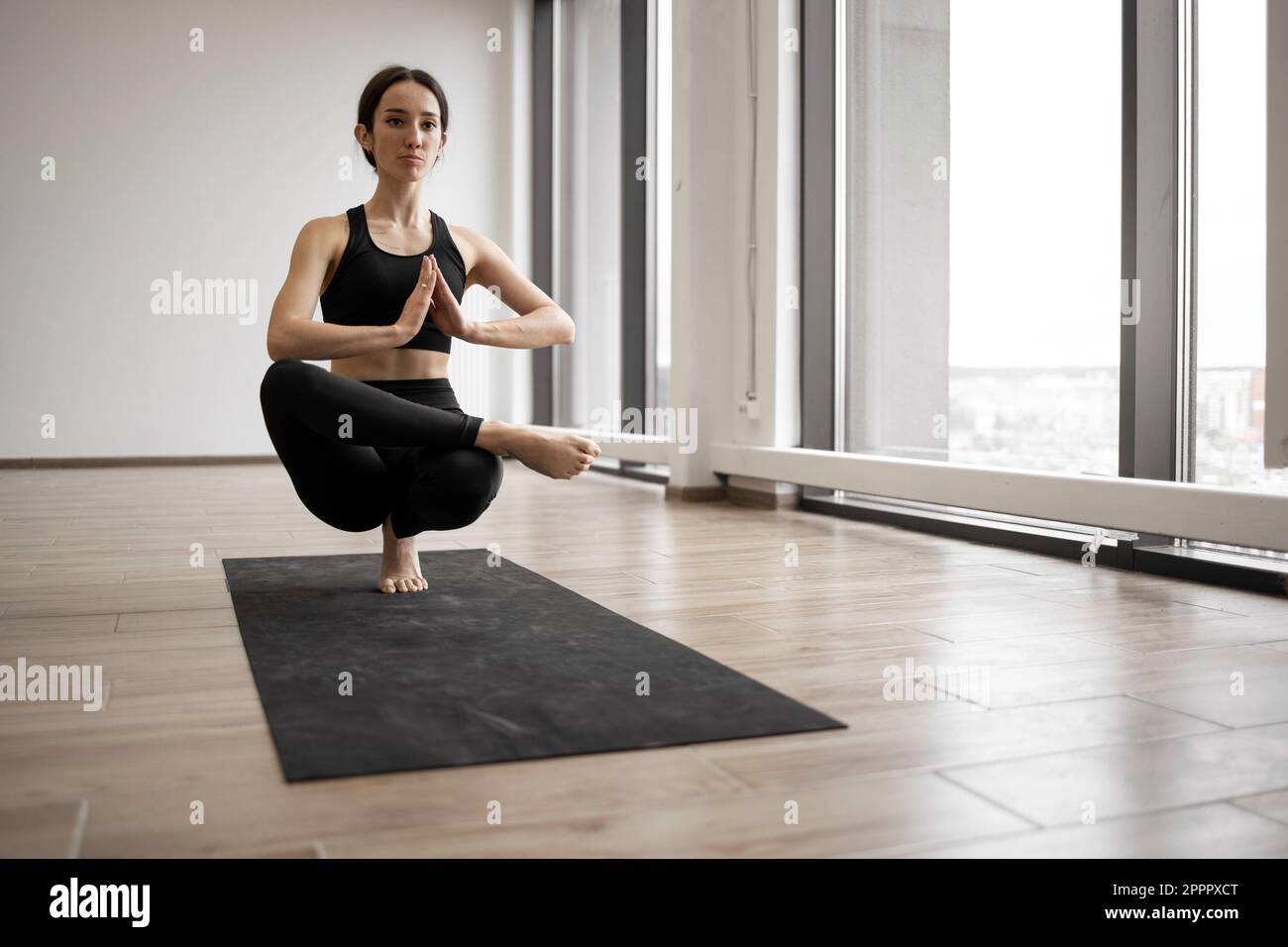 Strong active lady balancing on one leg and keeping hands in namaste ...