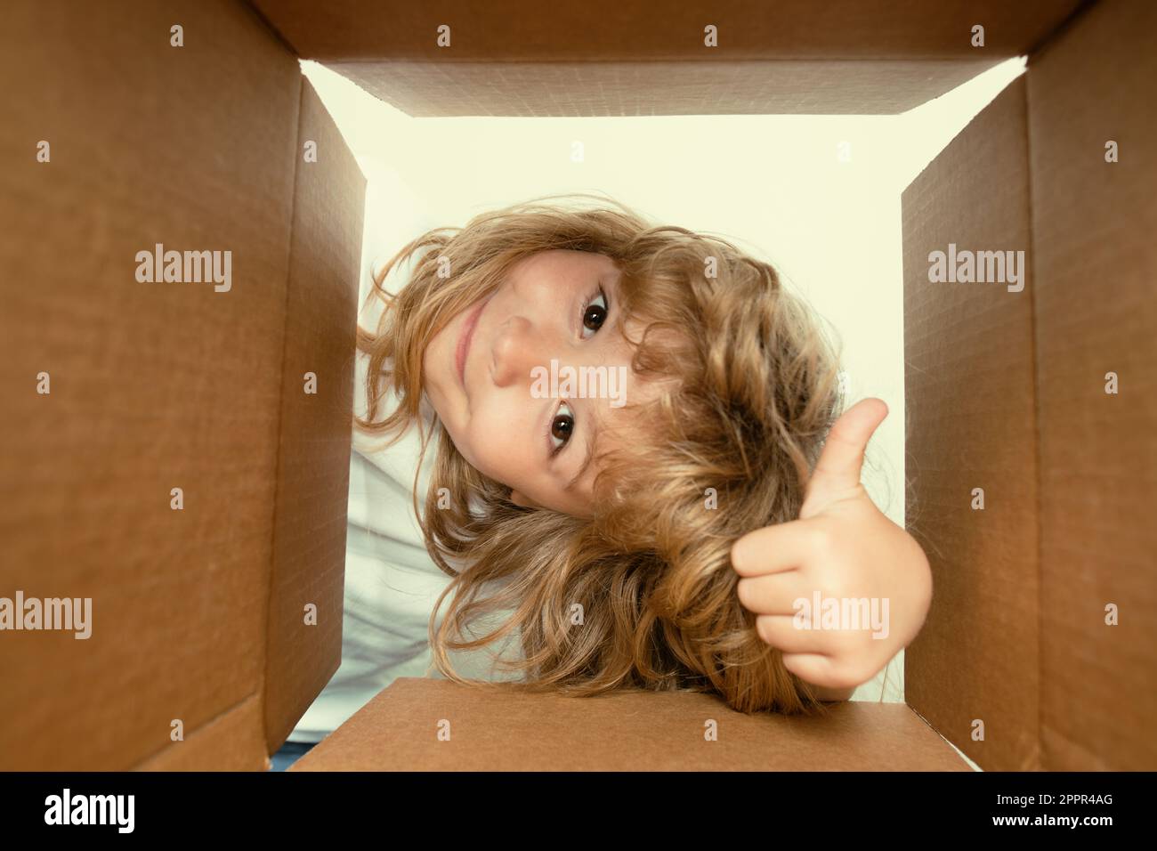 Surprised child boy with thumb up unpacking, opening carton box and ...