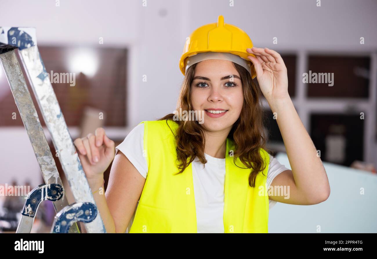 Smiling young female architect in yellow uniform at construction site ...