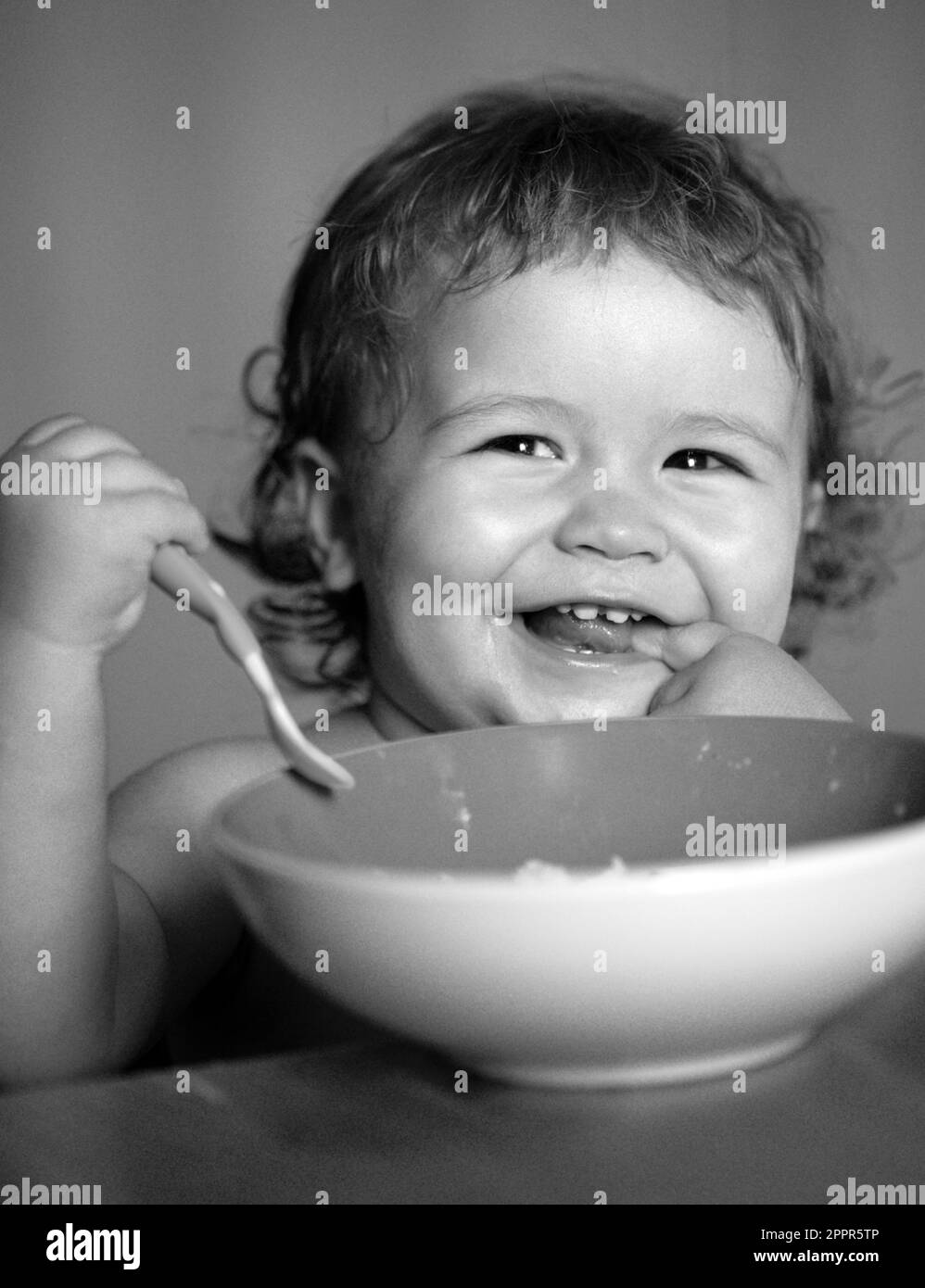 Smiling baby eating food. Funny baby eating food himself with a spoon ...