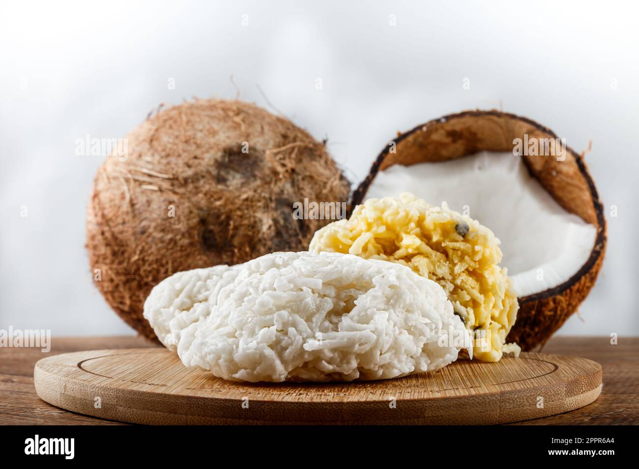 White and yellow cocada on wooden table with two coconuts behind and ...