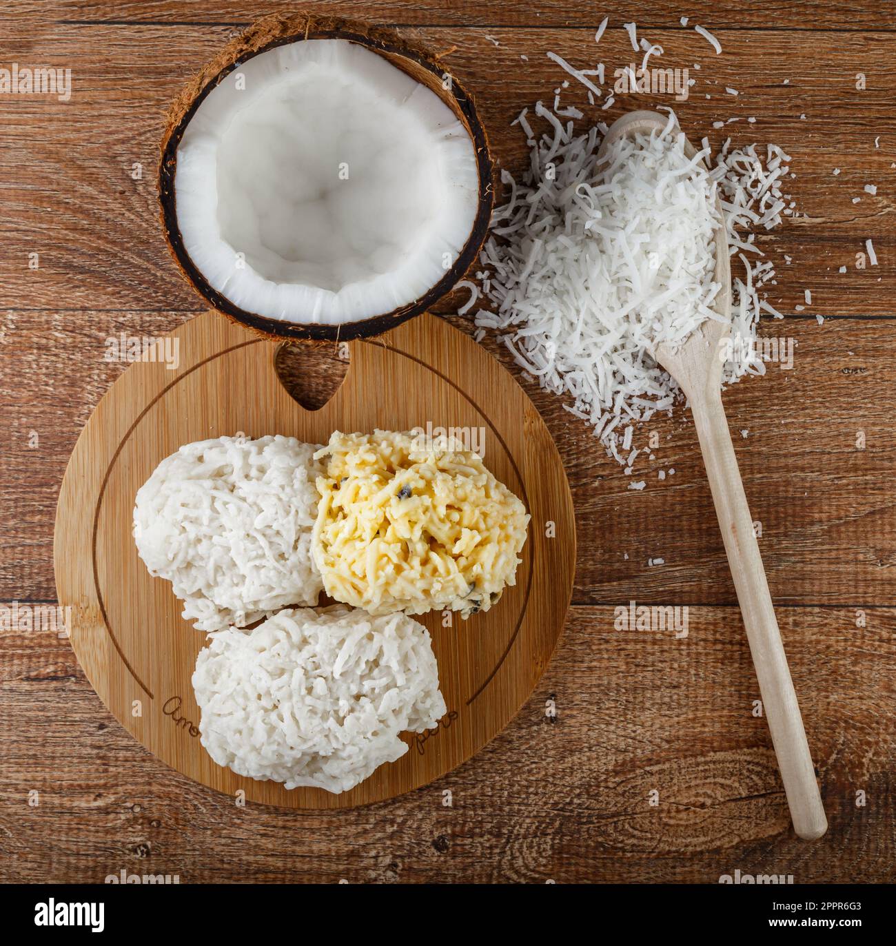 White and yellow cocada on wooden table with coconut and wooden spoon with grated coconut, love ...