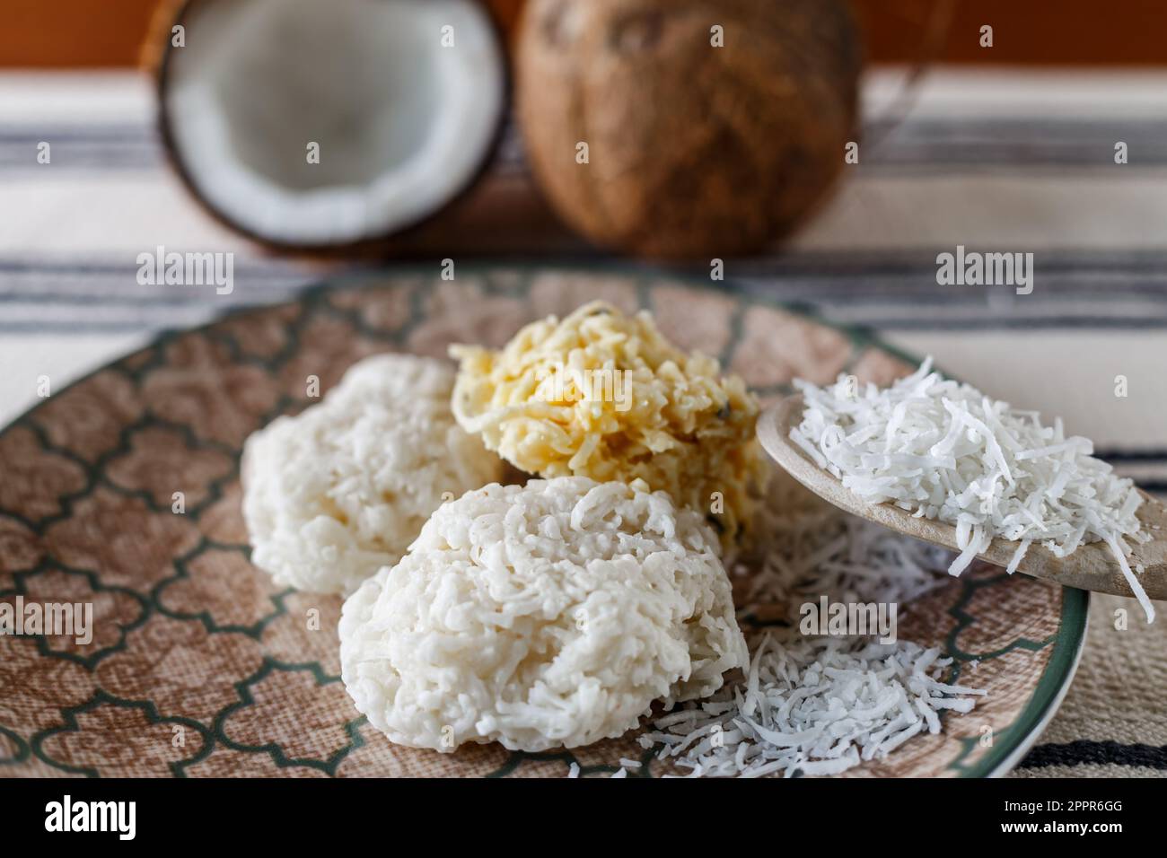 White and yellow cocada on wooden table with wooden spoon with grated coconut - top and ...