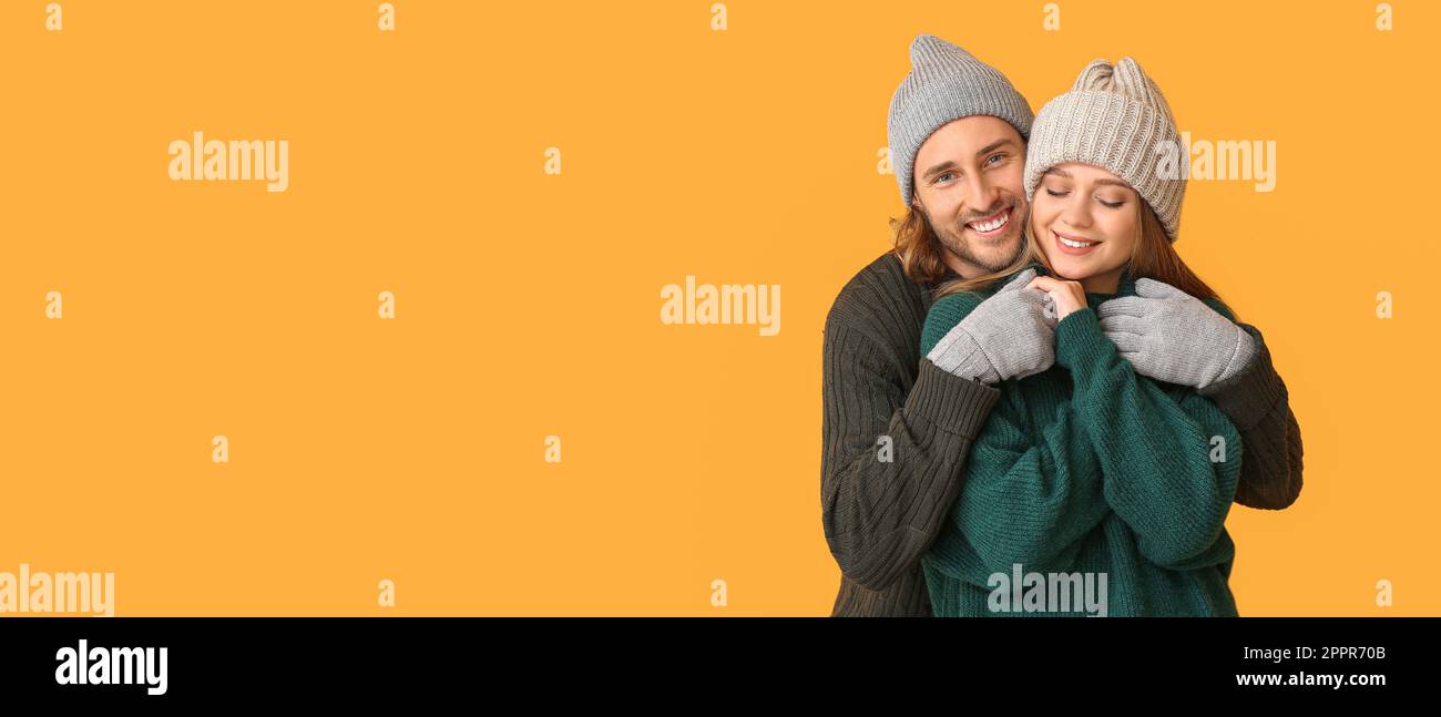 Happy couple in winter clothes on orange background with space for text ...