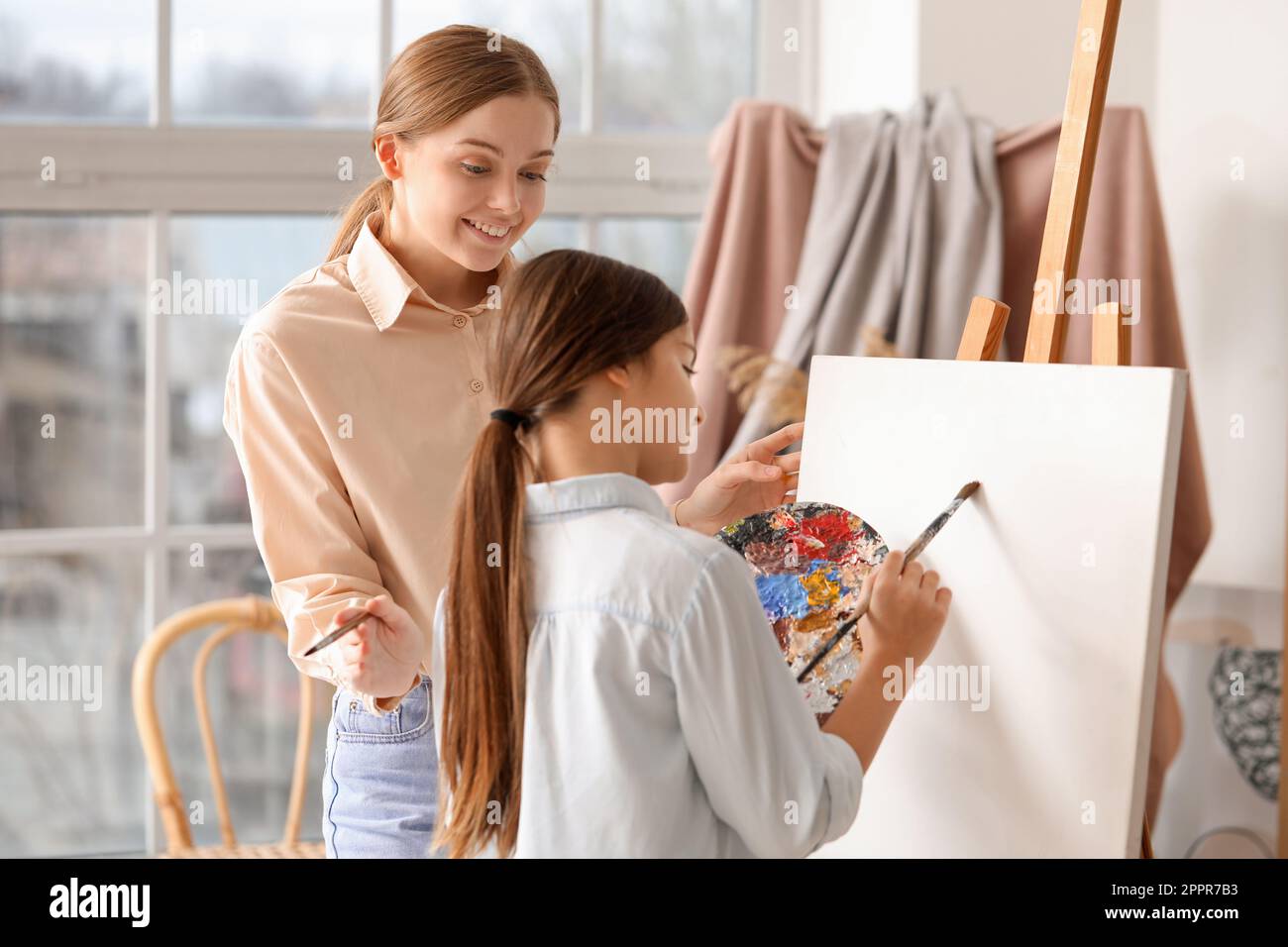 Drawing teacher giving private art lesson to little girl near easel in ...