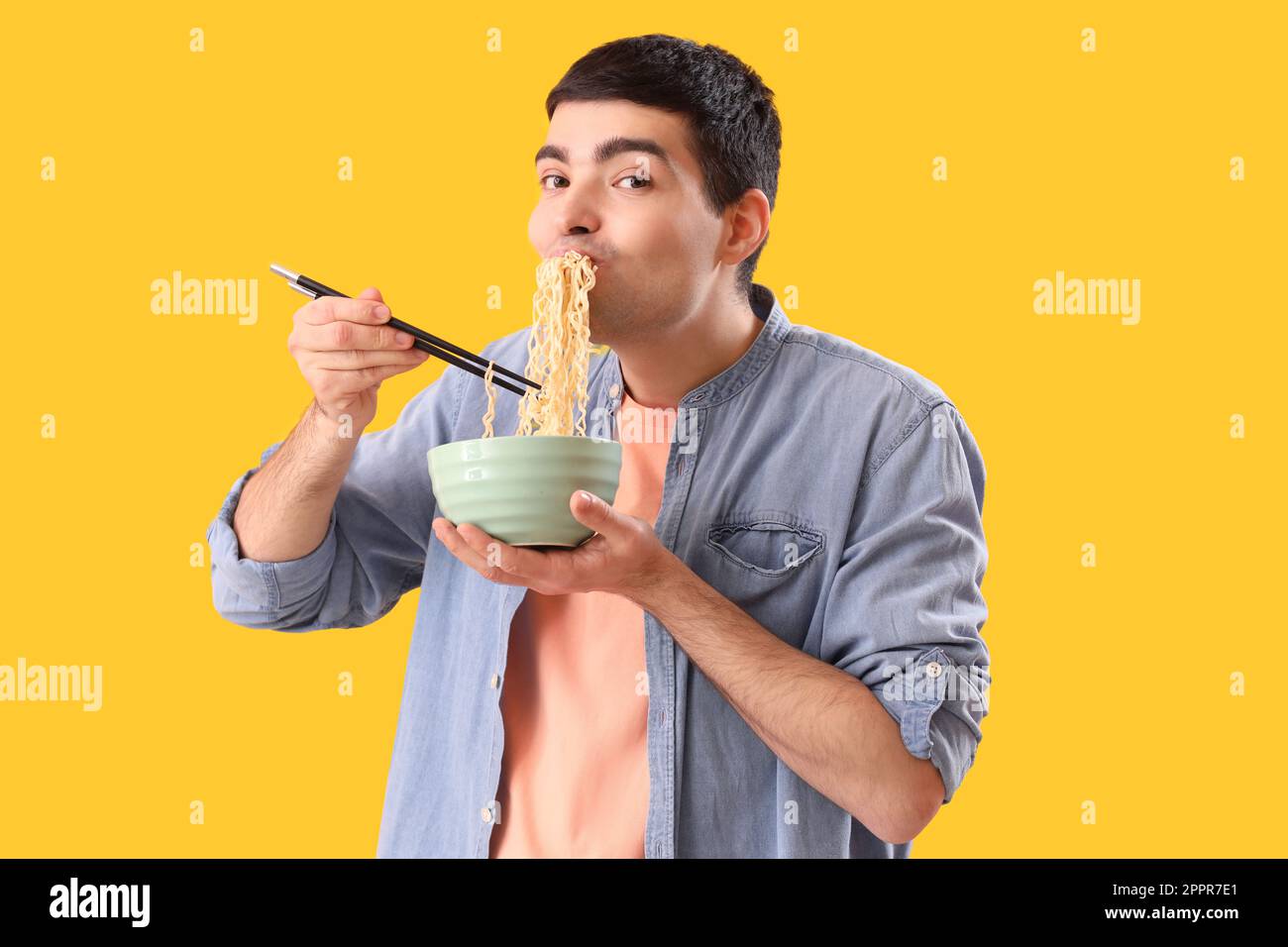 Young man eating Chinese noodles on yellow background Stock Photo - Alamy