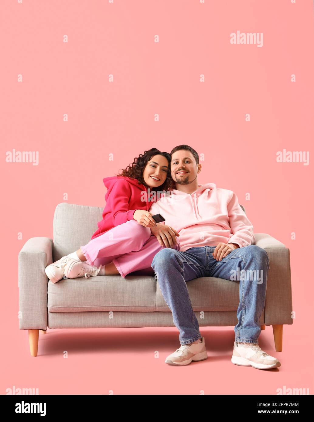 Young couple watching TV on pink background Stock Photo - Alamy