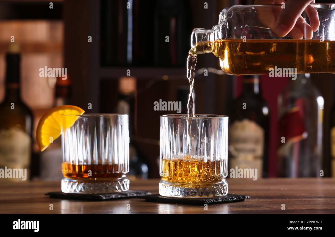 Pouring of cold rum from bottle into glasses at table in bar Stock ...