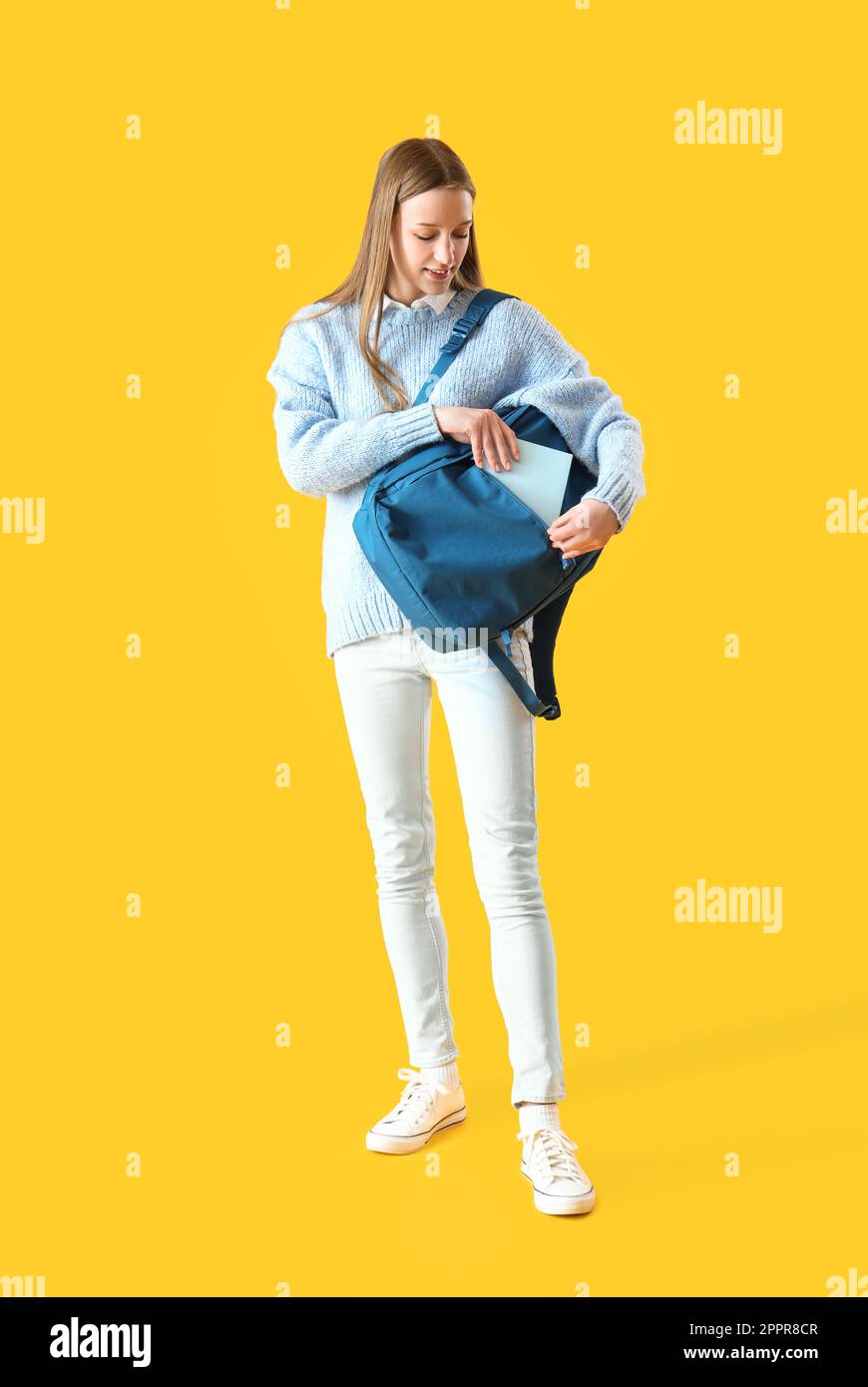 Female student putting copybook into backpack on yellow background ...